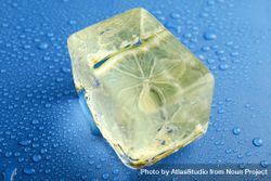 Top view of large rectangular ice cube with lemon slice on blue table ...
