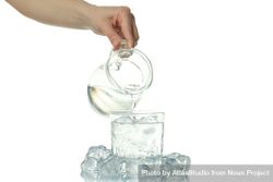 Hand pouring pitcher of water being poured into glass surrounded by ice ...